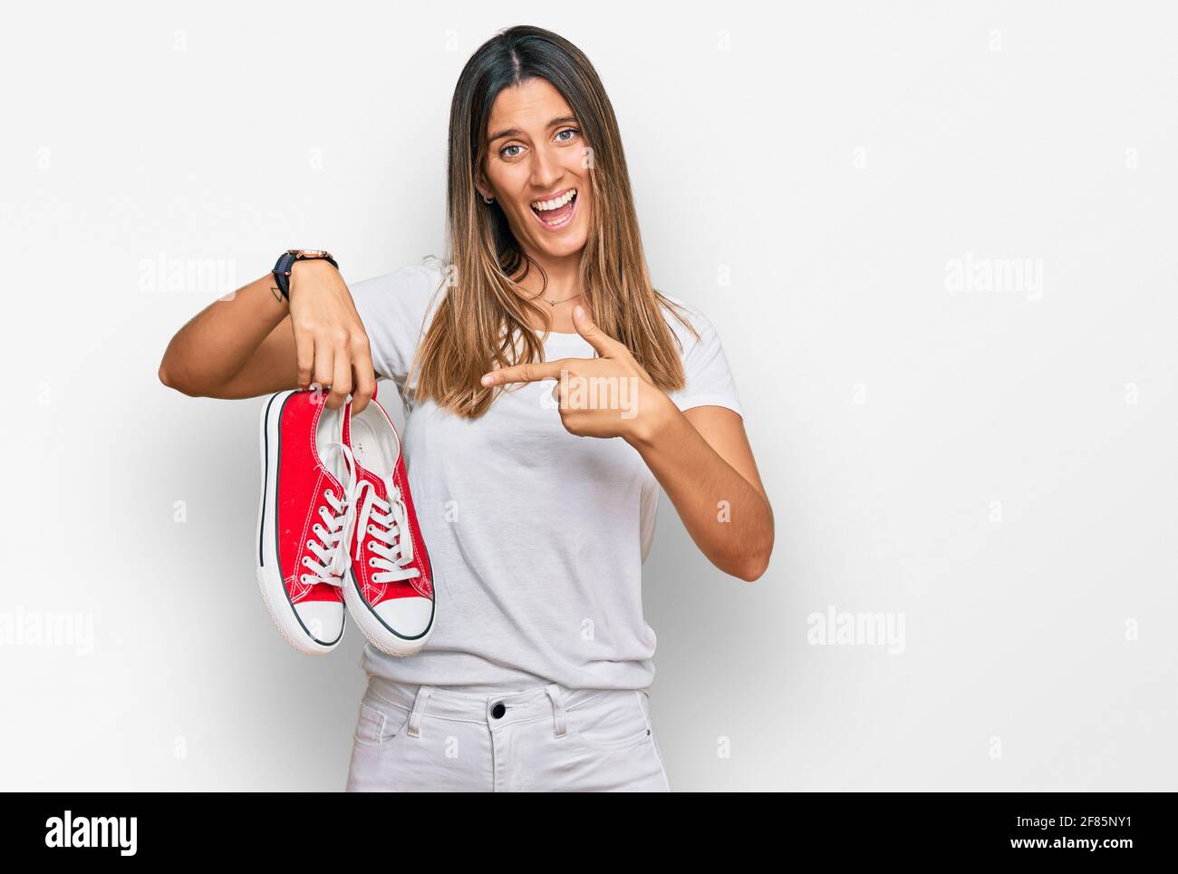 Young woman holding red casual shoes smiling happy pointing with hand ...
