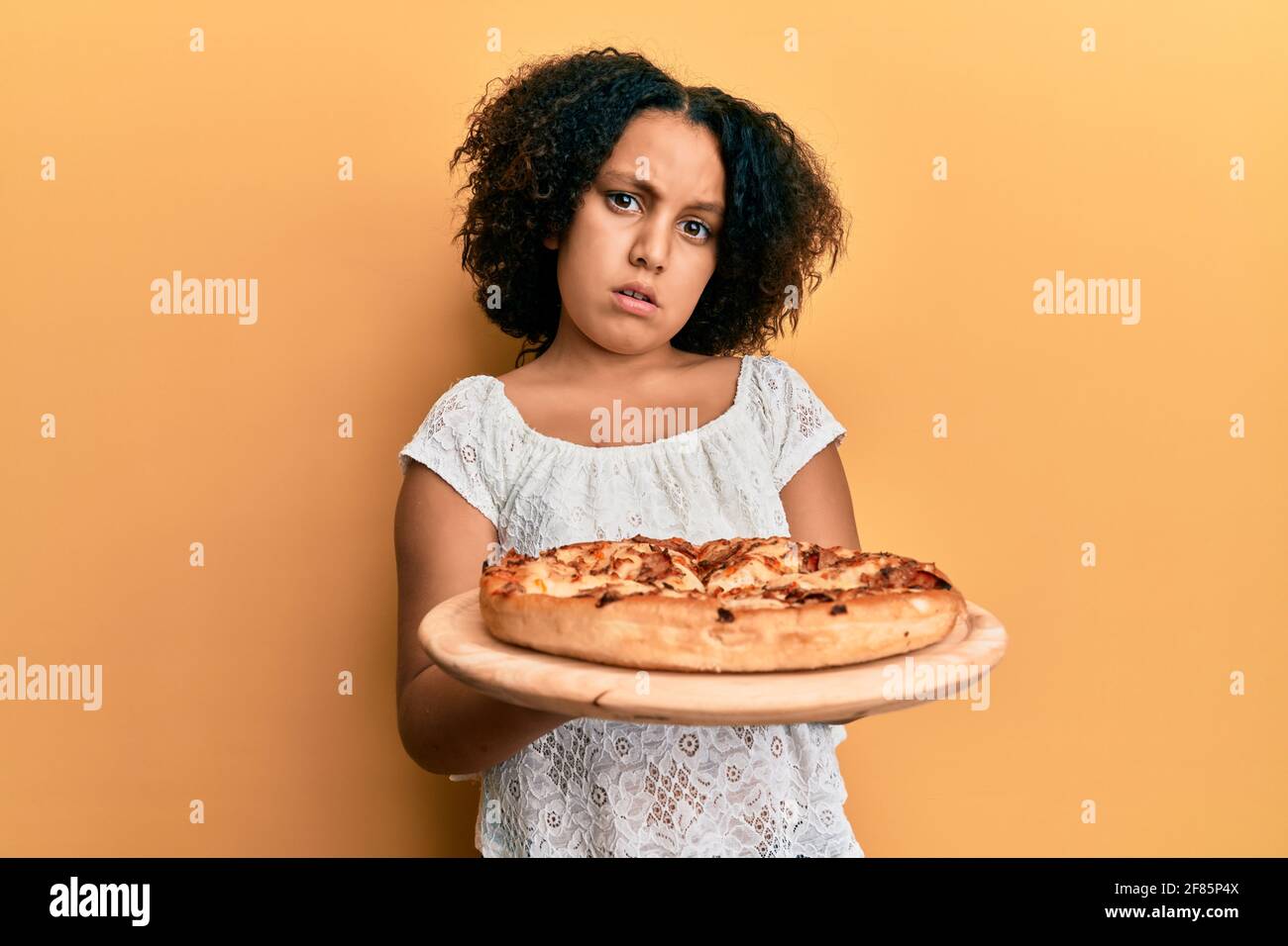 Young little girl with afro hair holding italian pizza in shock face ...