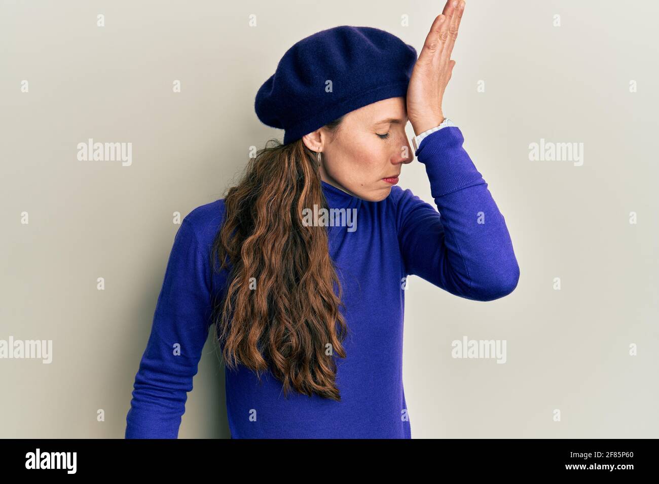 Young blonde woman wearing french look with beret surprised with hand ...
