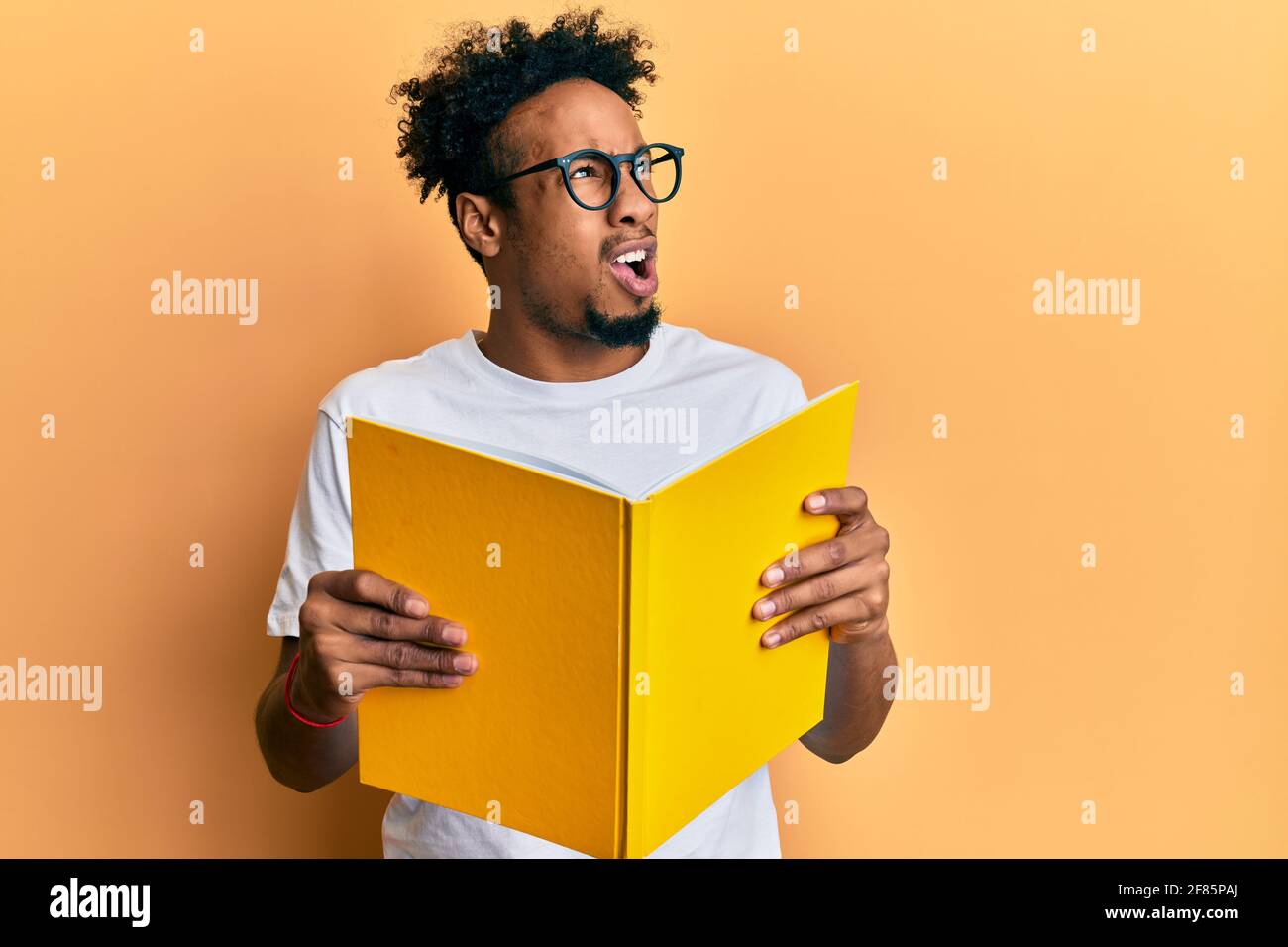 Young african american man with beard reading a book wearing glasses ...