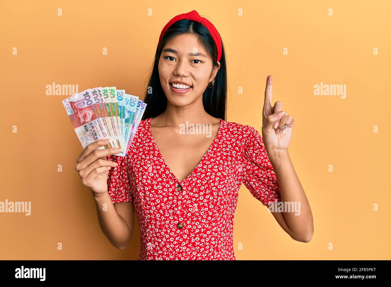 Young chinese woman holding hong kong dollars banknotes smiling with an ...