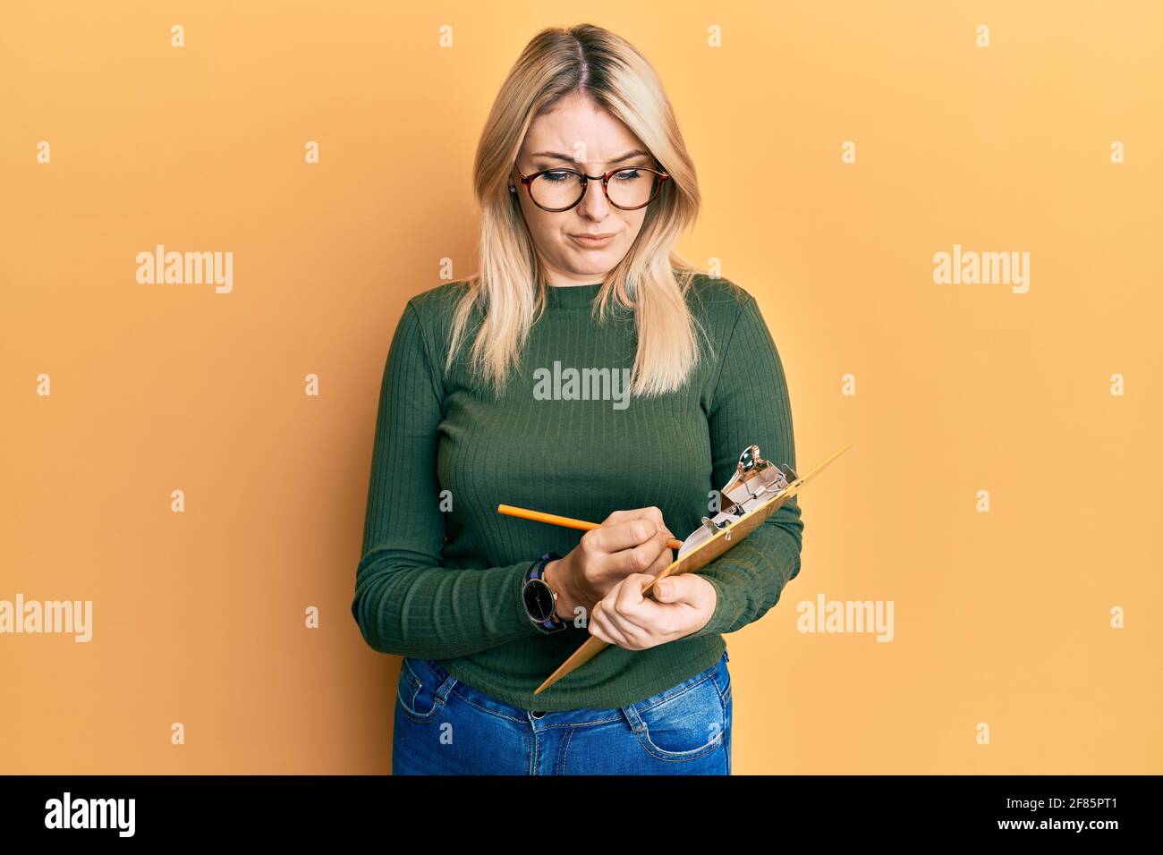 Young caucasian woman writing on checklist clipboard skeptic and ...
