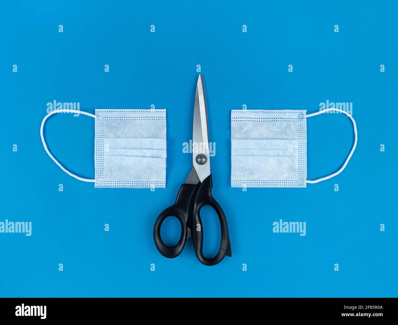 Medical disposable face mask cut in half and scissors on a blue ...