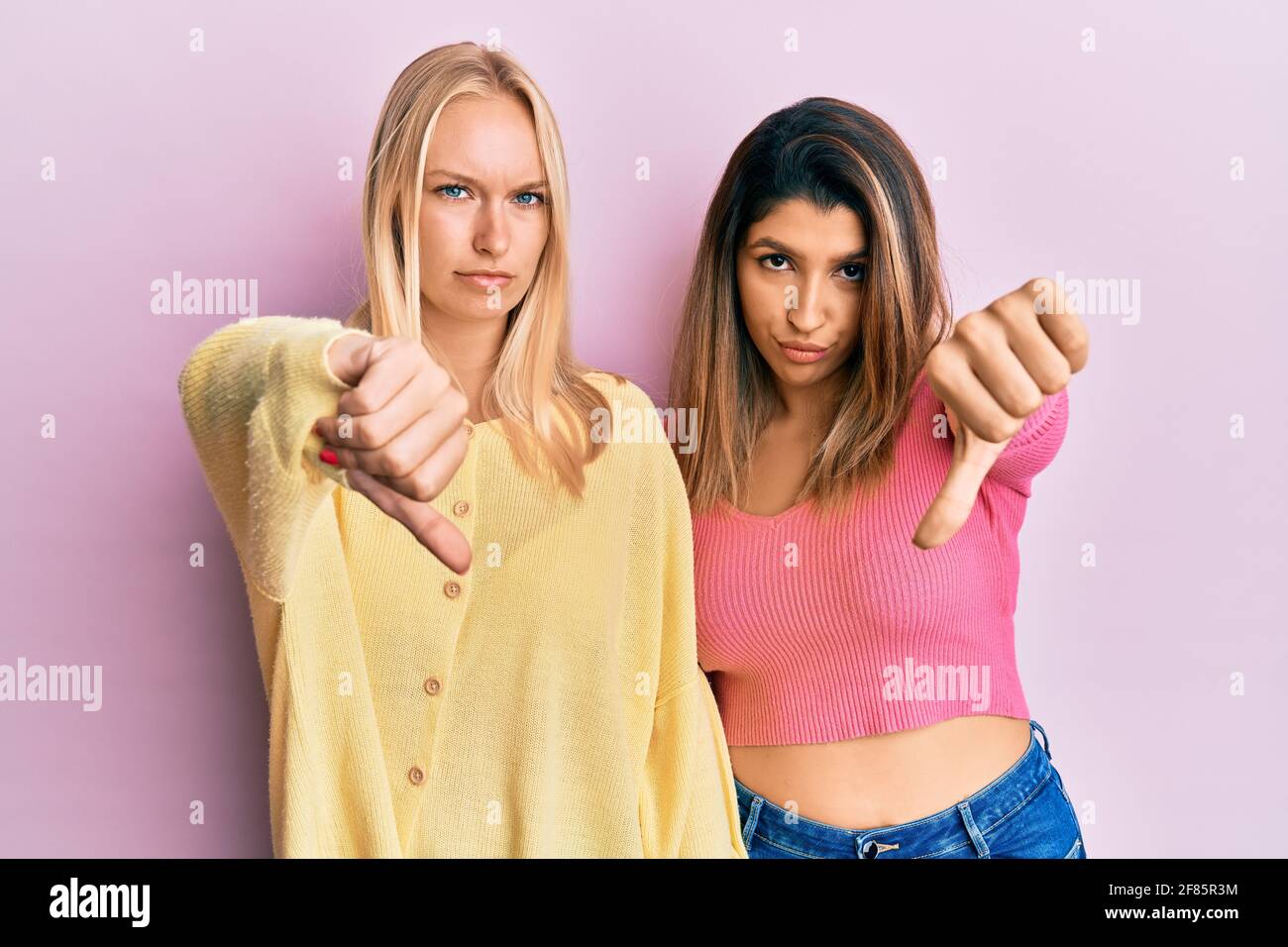Two friends standing together over pink background looking unhappy and ...