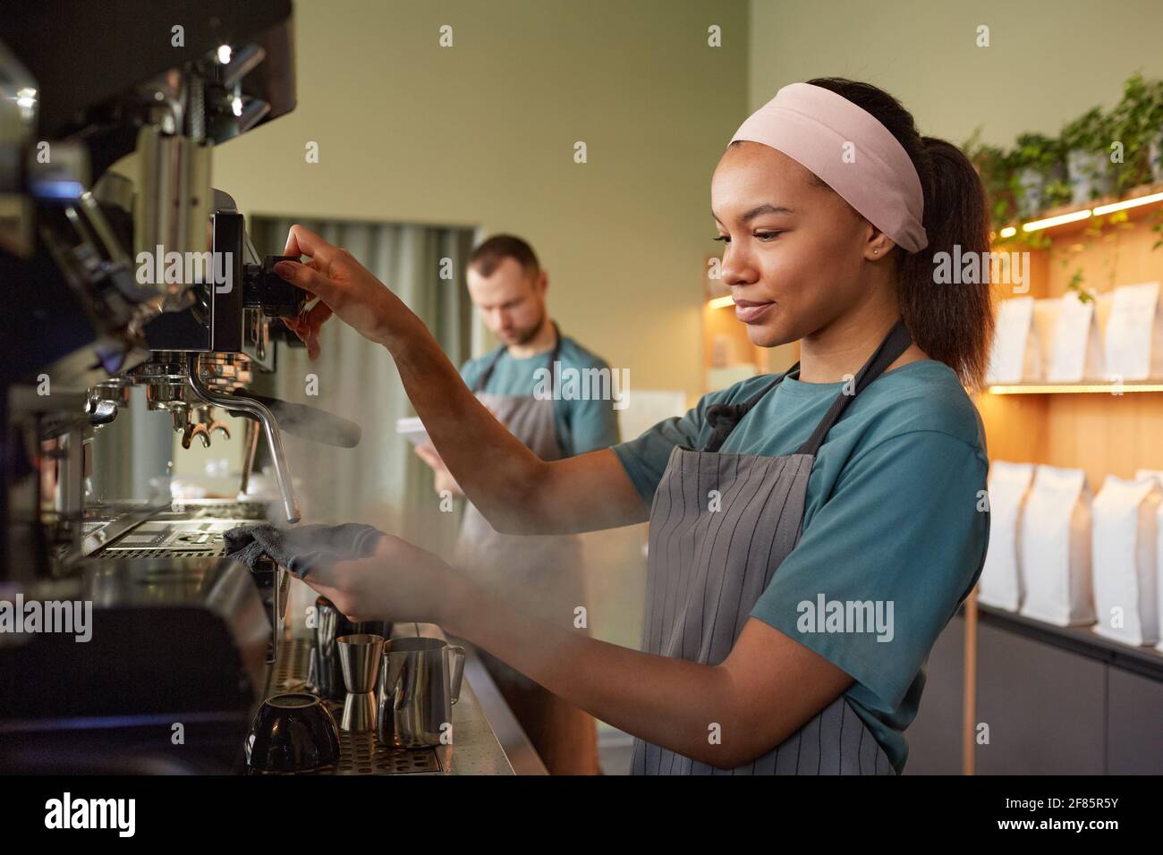 Side view portrait of young female barista making fresh coffee in cafe ...
