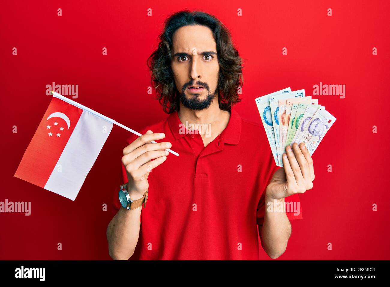 Young hispanic man holding singapore flag and dollars clueless and ...