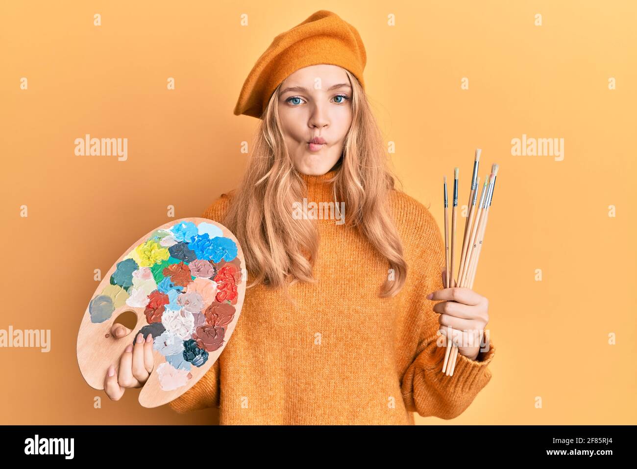Beautiful young caucasian girl holding paintbrush and painter palette ...