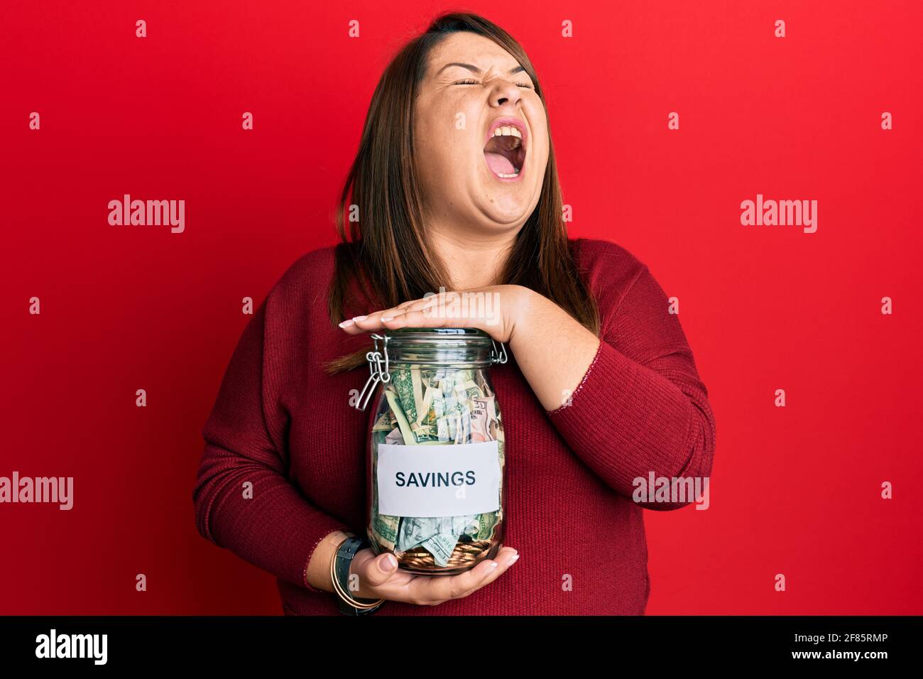 Beautiful brunette plus size woman holding jar with savings angry and ...