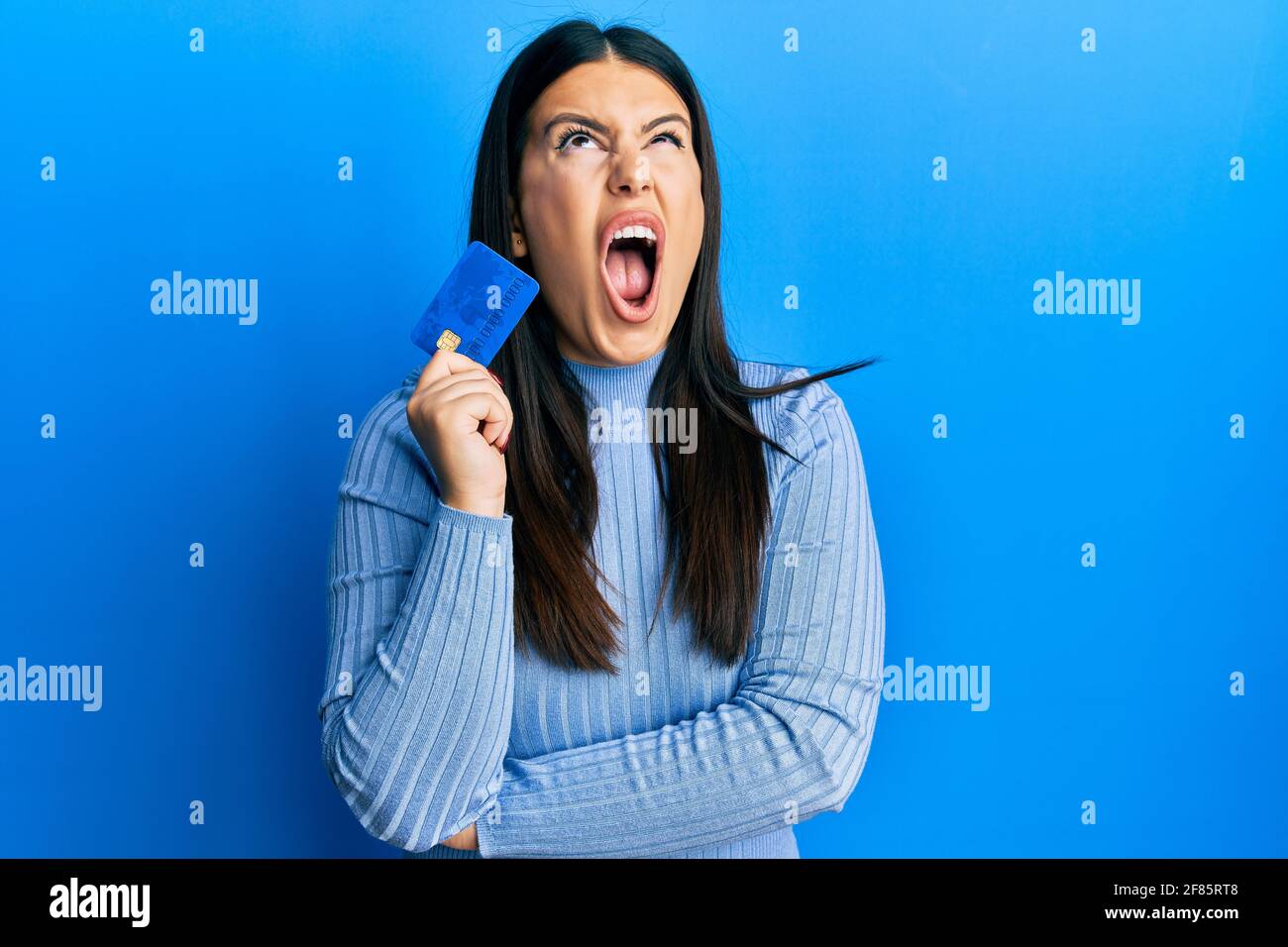Beautiful brunette woman holding credit card angry and mad screaming ...