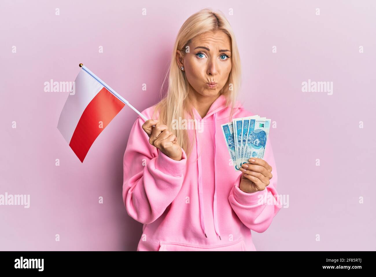 Young blonde woman holding poland flag and zloty banknotes depressed ...