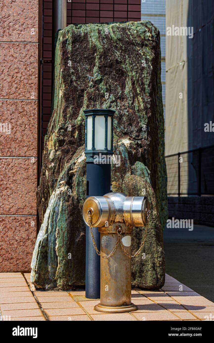 A fire hydrant, a lamp and a standing rock, sit in a row next to the ...
