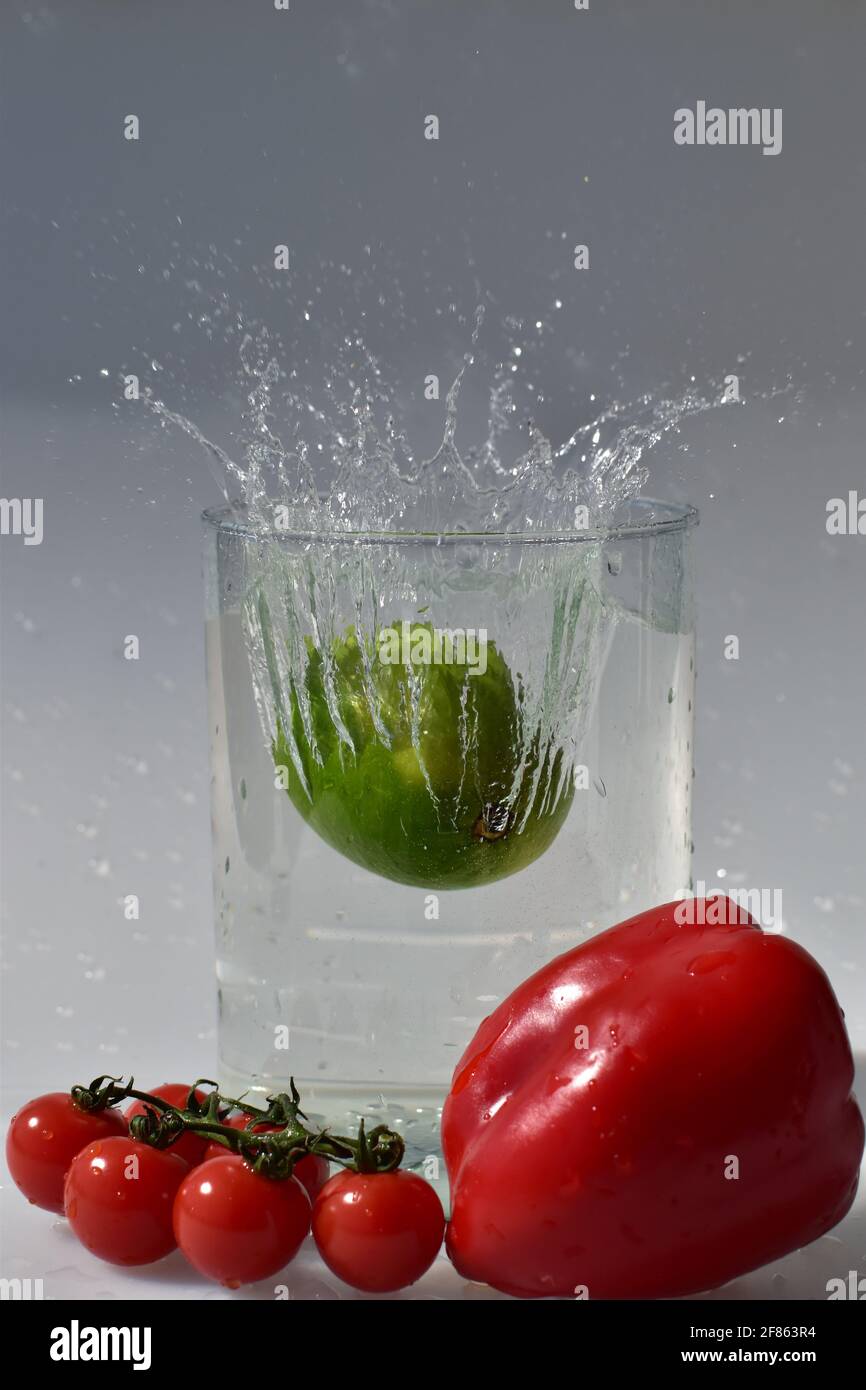 Vertical shot of vegetables fallen into a glass jar causing water ...