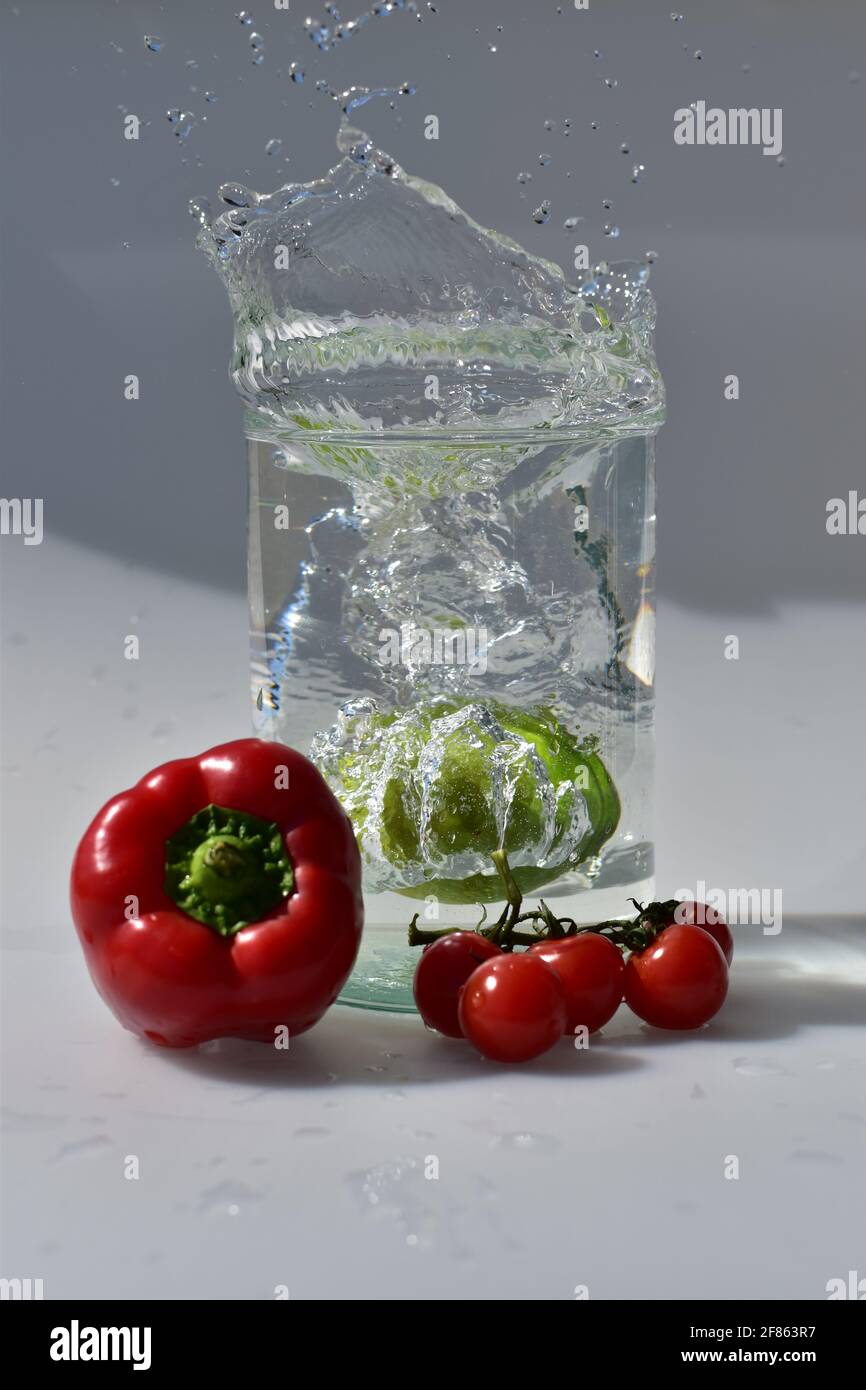 Vertical shot of vegetables fallen into a glass jar causing water ...