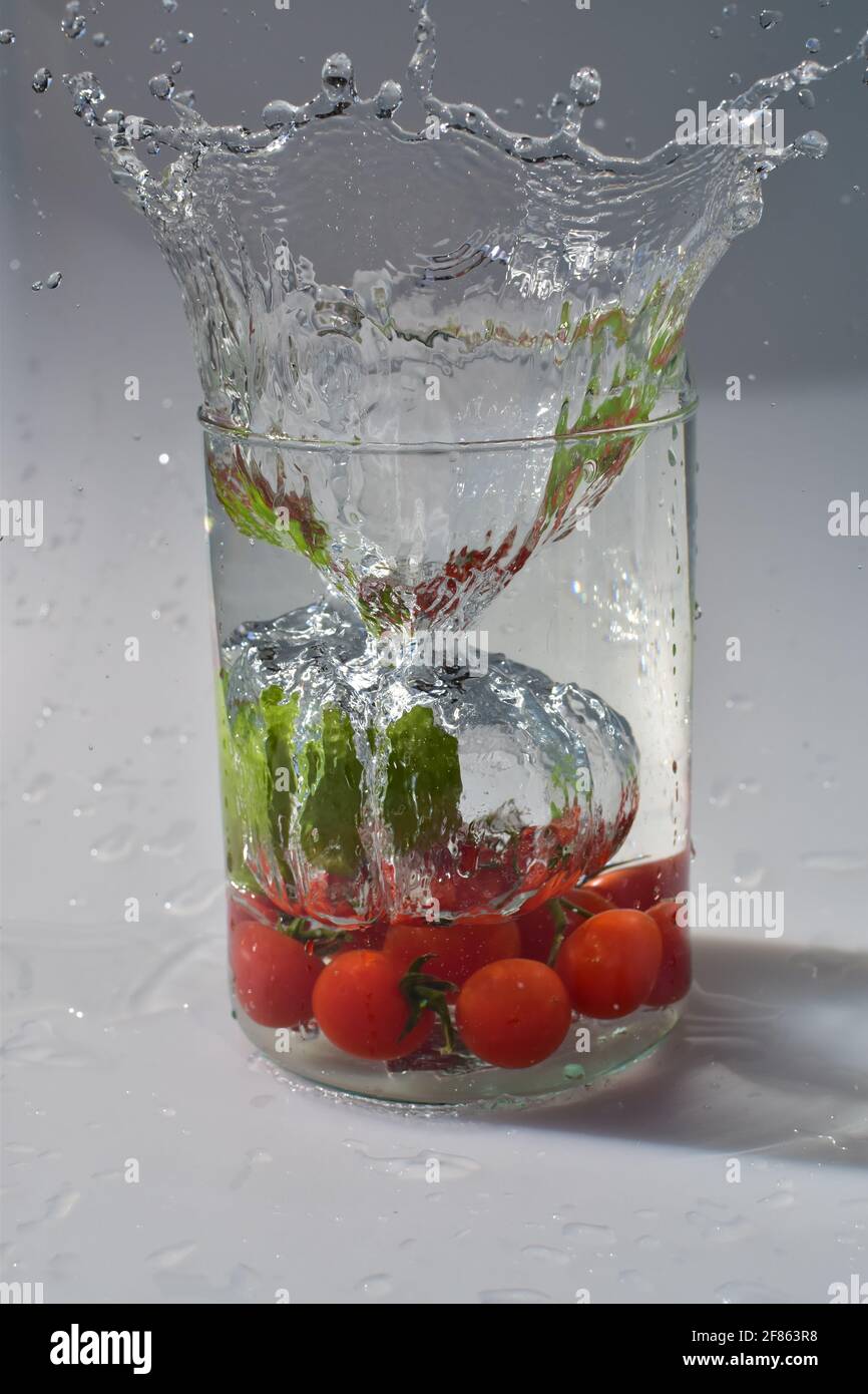 Vertical shot of vegetables fallen into a glass jar causing water ...