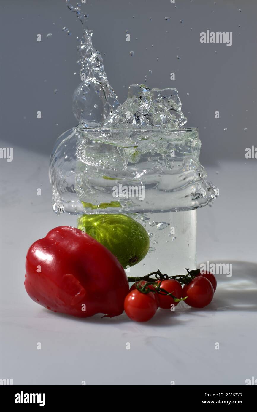 Vertical shot of vegetables fallen into a glass jar causing water ...