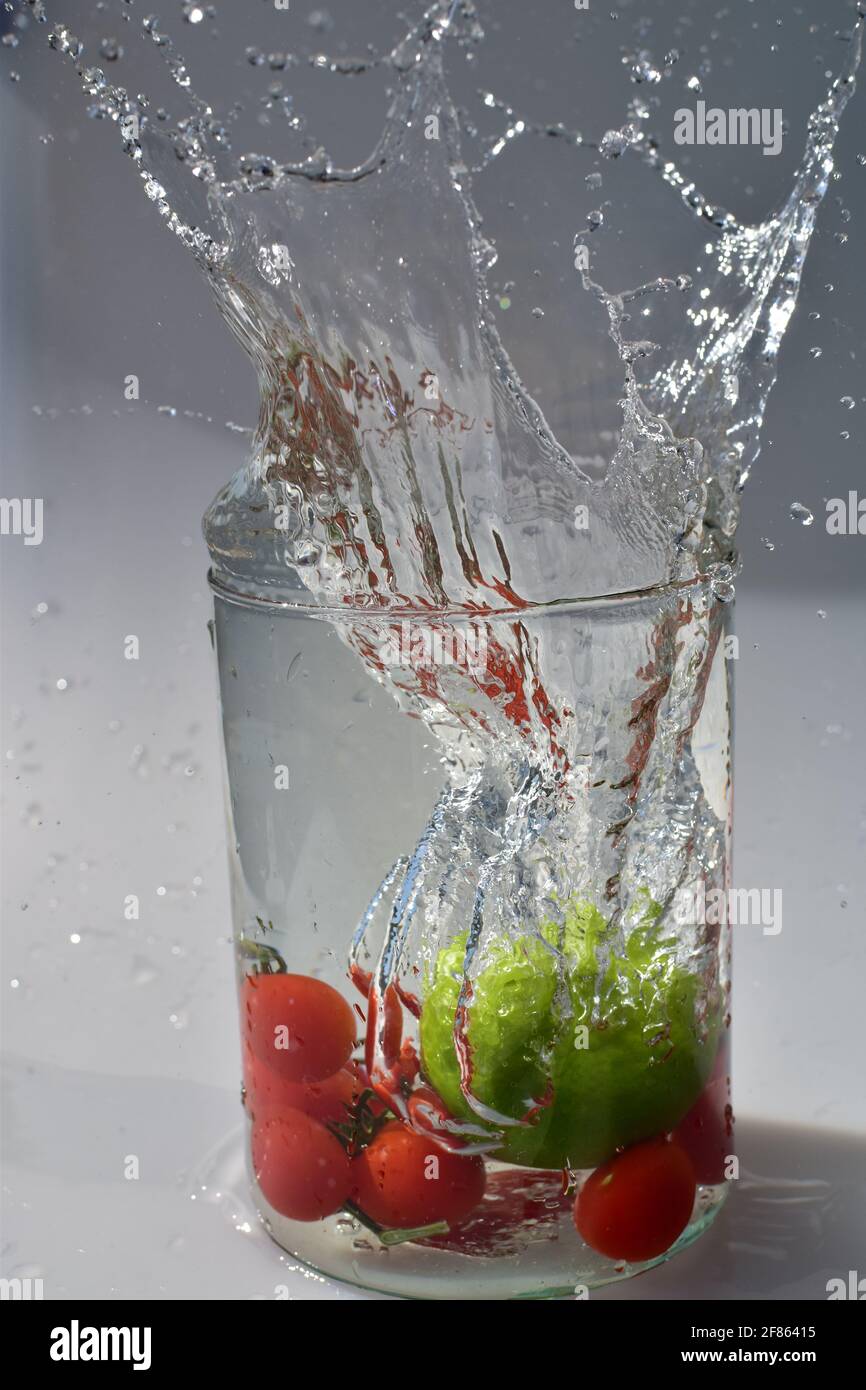 Vertical shot of vegetables fallen into a glass jar causing water ...