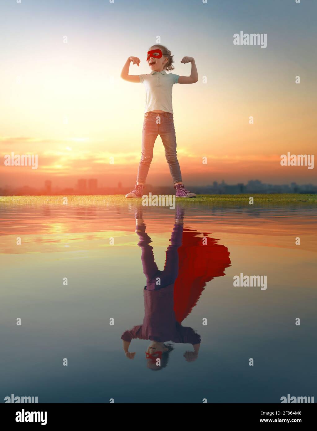 Little child playing superhero and looking at her reflection in water ...