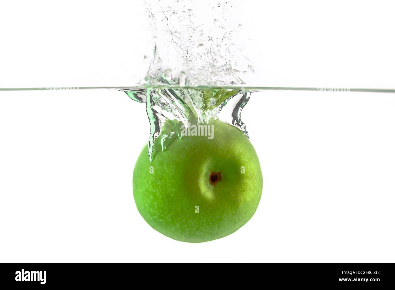 one green apple falling into water on a white background with splashes ...