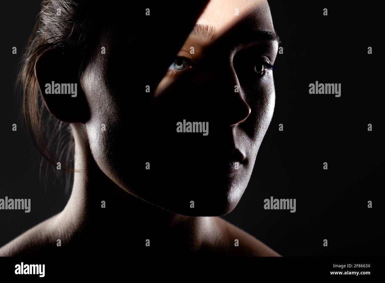 studio portrait of a beautiful young woman with shadows on her face ...