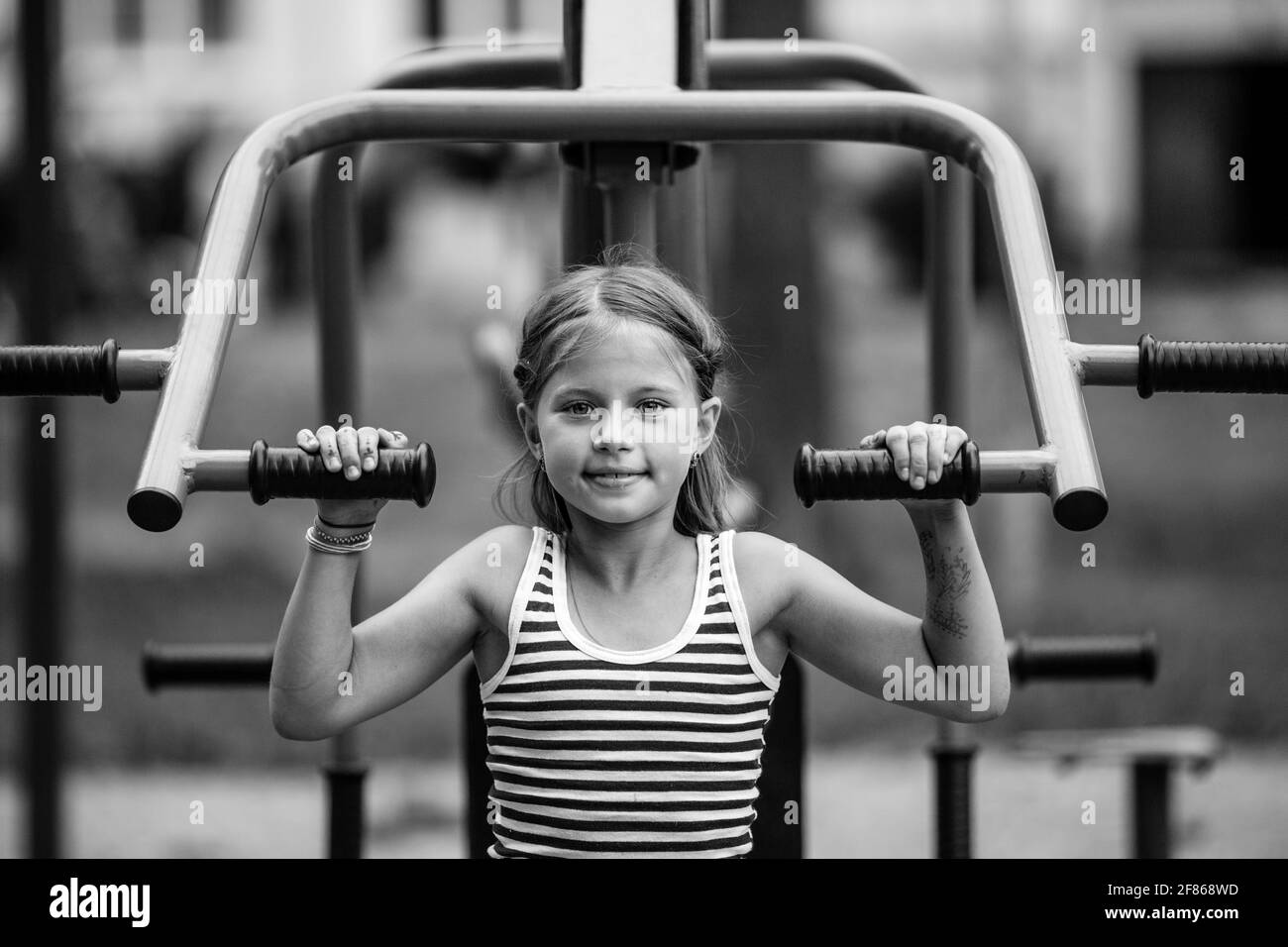 Portrait of little girl on a trainer-machine outdoors. Black and white ...