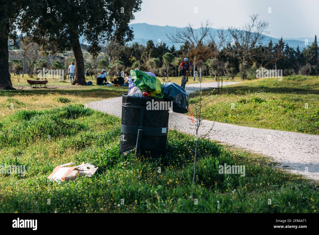 Loaded trash can and rubbish thrown on the grass in a park Stock Photo ...