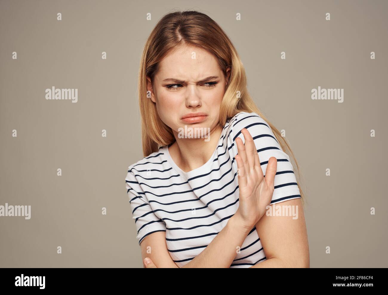 Blond woman with disgust looks to the side and beige background cropped ...