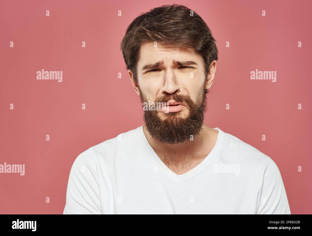 Portrait of an upset man in a white t-shirt on a pink background ...