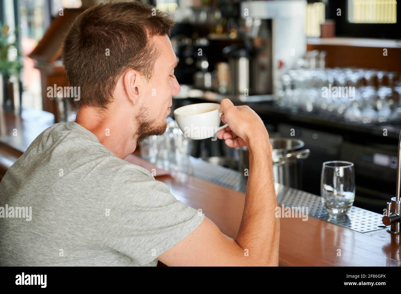 Back view of handsome young man sitting on bar and drinking cup coffee ...