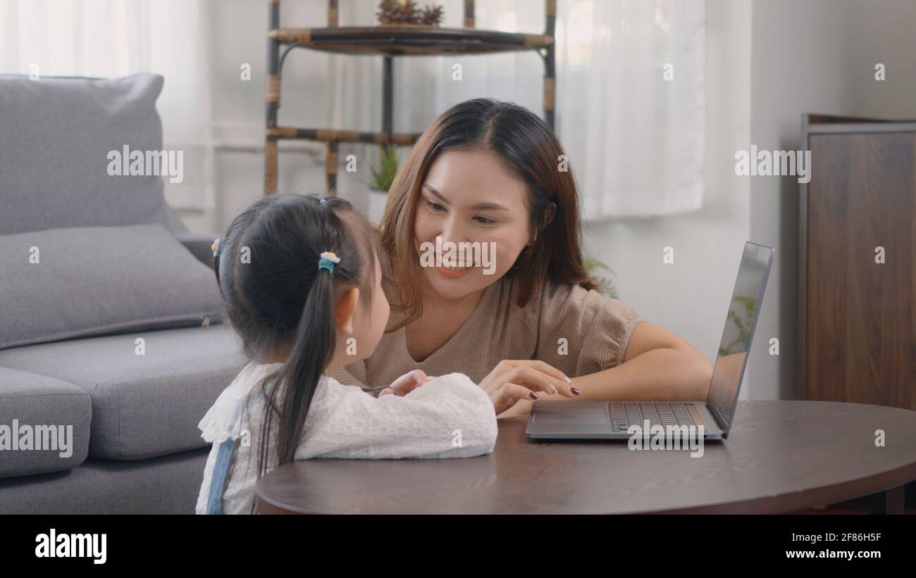 Asian young mother with laptop computer teaching her kid to learn or ...