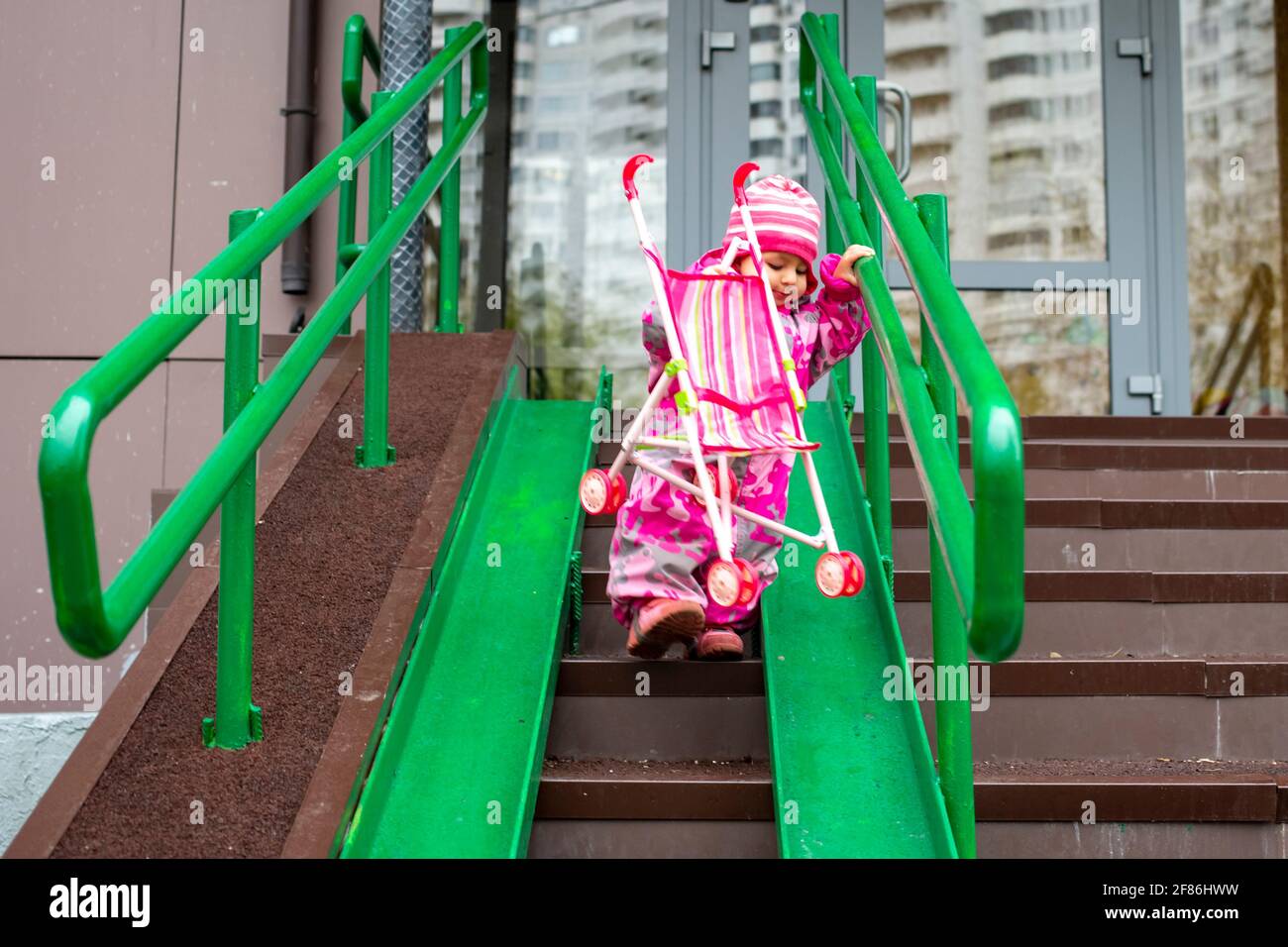 cute toddler with a toy stroller walks along steel railing ramp for ...