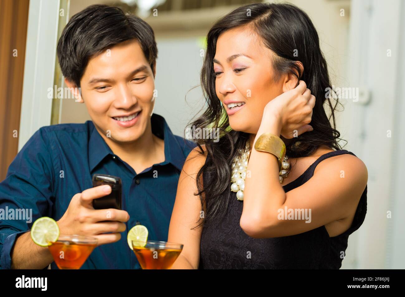 Asian man is flirting with woman in a bar while having drinks, woman is ...