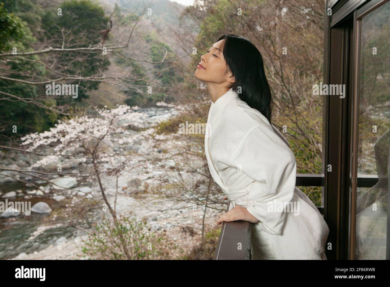 Beautiful carefree young woman in bathrobe on balcony overlooking river ...