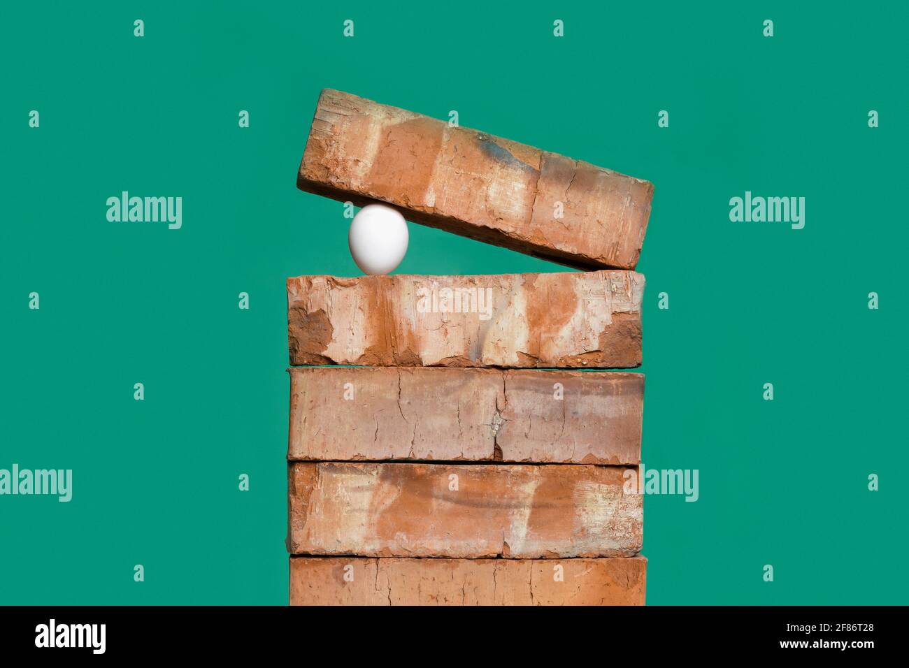 Egg between bricks on green background Stock Photo - Alamy
