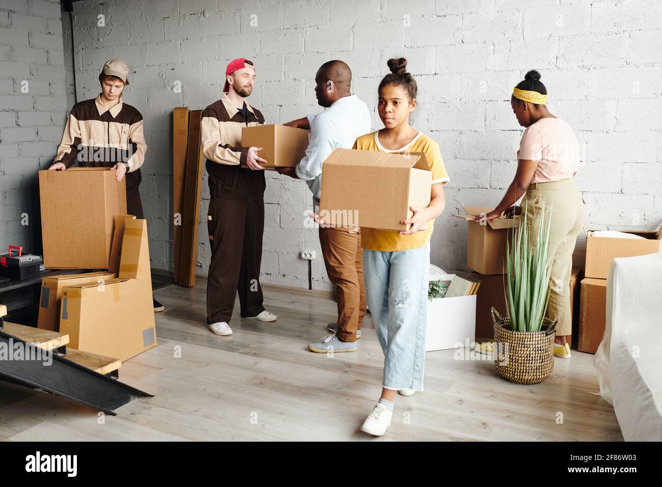 Pretty teenage girl of African ethnicity carrying packed cardboard box ...