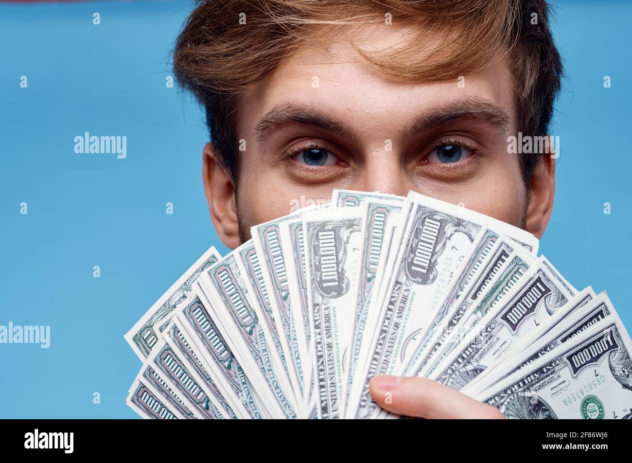 a man with a wad of money covers his face close-up blue background ...