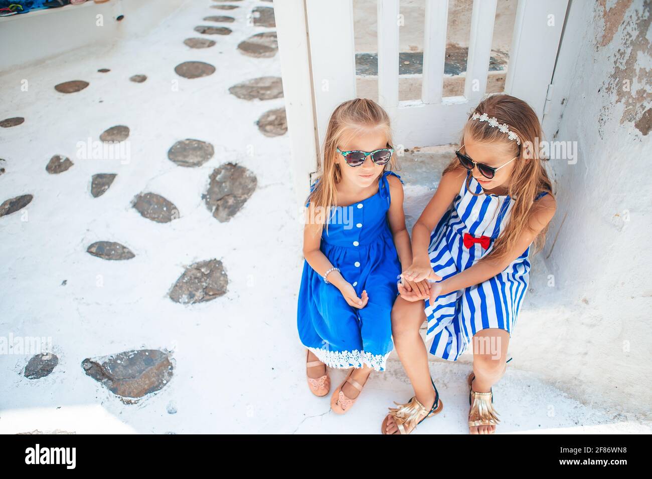 Little happy girls in dresses at street of typical greek traditional ...