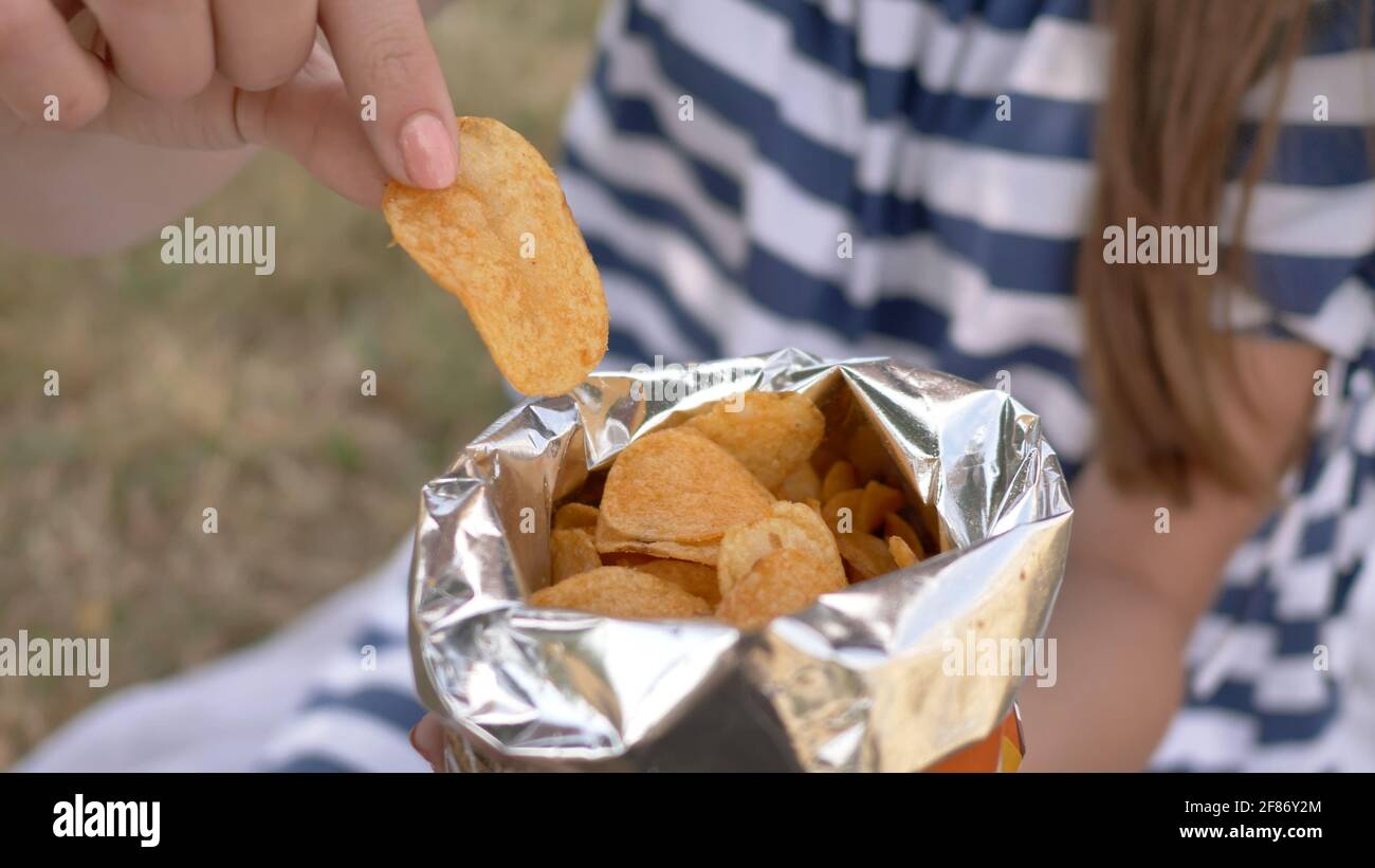 The girl eats chips in the city park in the summer. The girl eats chips ...