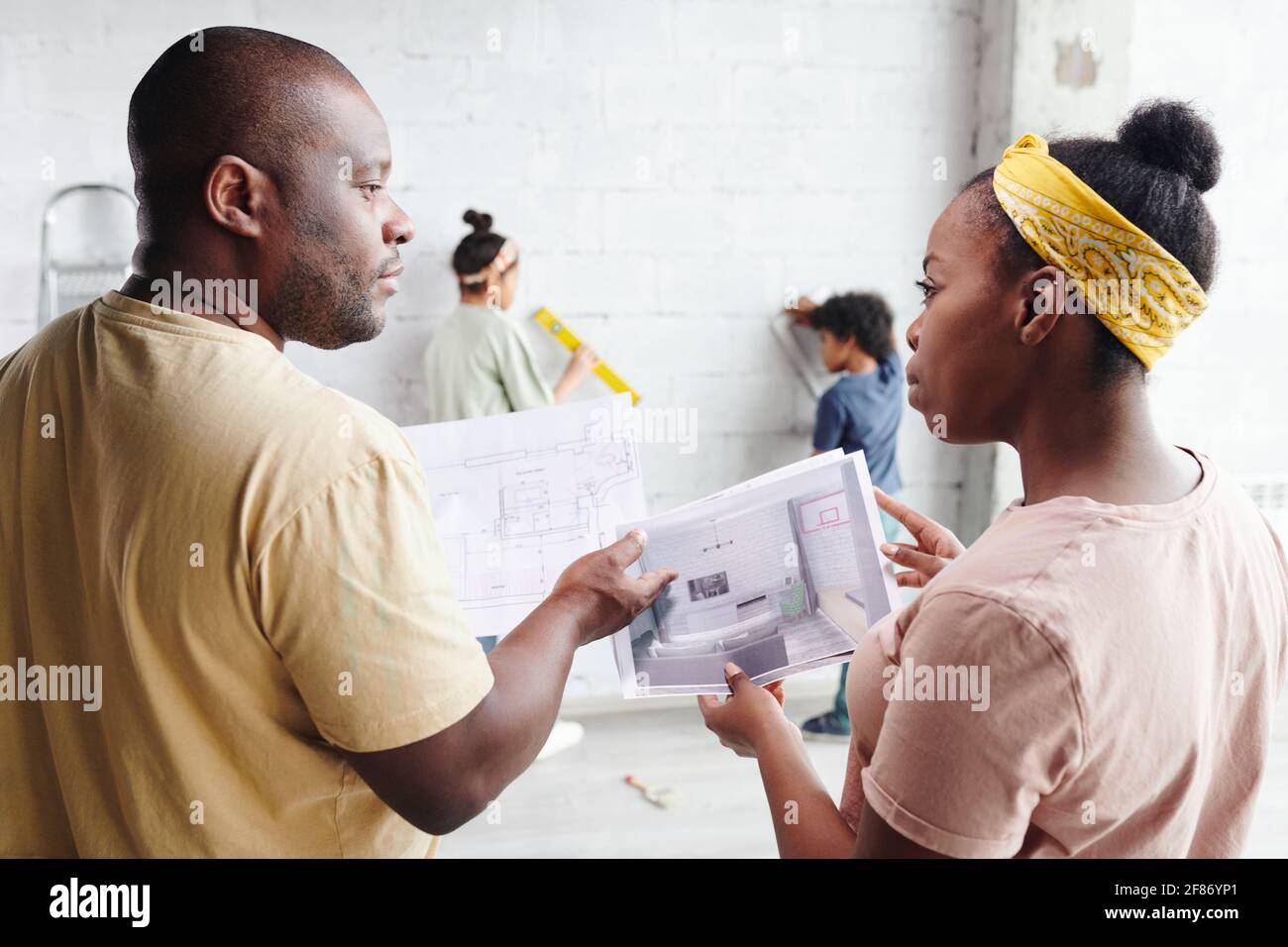 African couple in casualwear discussing papers with draft and interior ...