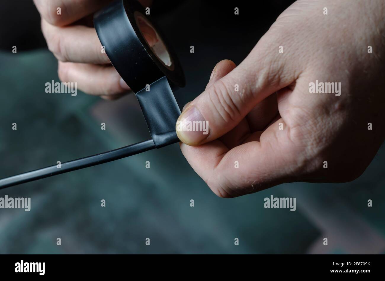 A man is insulating a black electrical wire. Close-up of male hands ...
