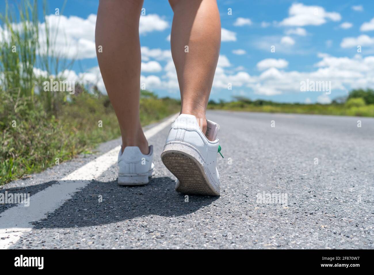Woman is walking on small country road street with blue sky background ...