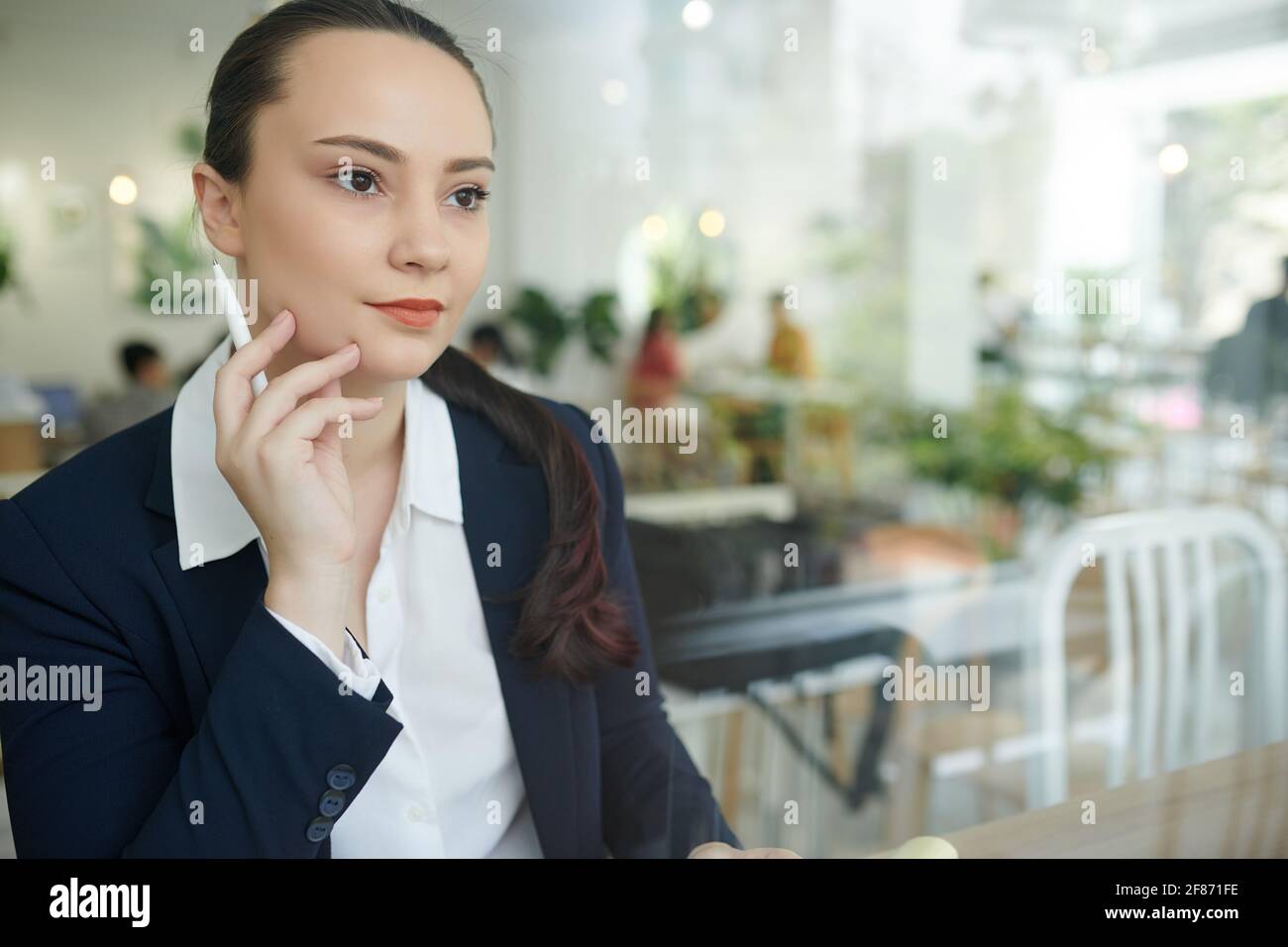 Portrait of beautiful pensive young businesswoman sitting at cafe table ...