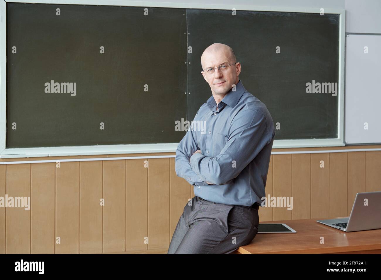 Bald professor of university in smart casualwear sitting on desk ...