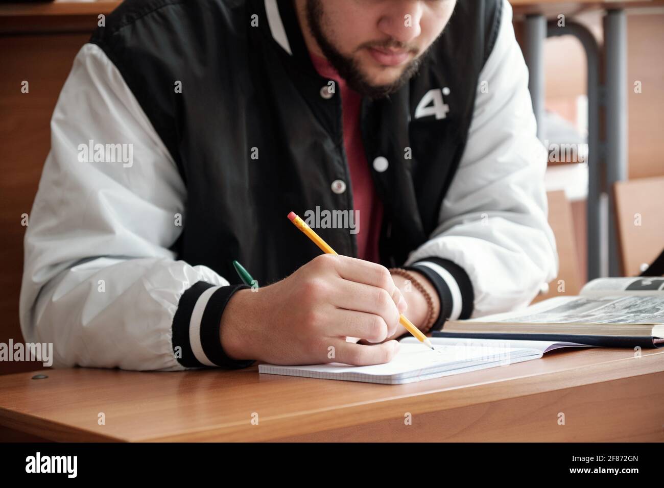 Hands of bearded guy in casualwear bending over desk and making notes ...