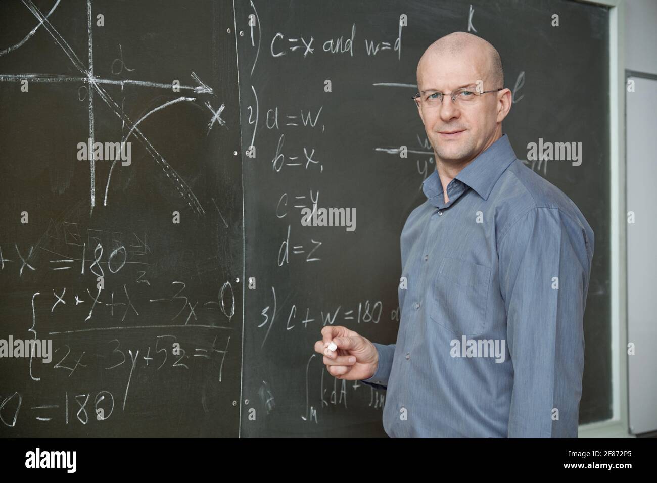 Mature bald professor in smart casualwear holding piece of chalk while ...