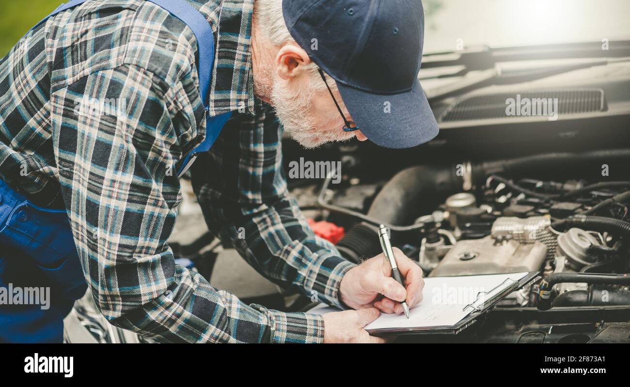 Car mechanic checking a car engine and writing on clipboard Stock Photo ...