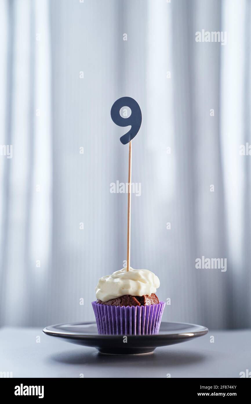 Tasty chocolate cupcake or muffin with number 9 nine on black plate ...