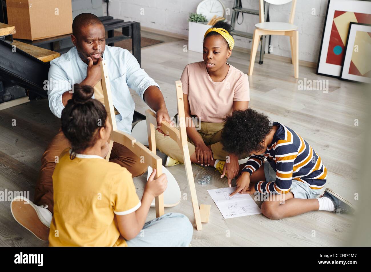 Puzzled African man looking at parts of wooden chair while going to ...