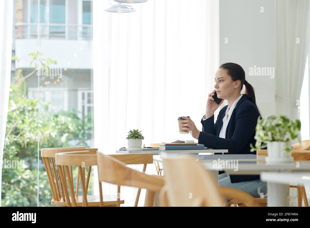 Pensive serious young businesswoman sitting at cafe table, drinking ...
