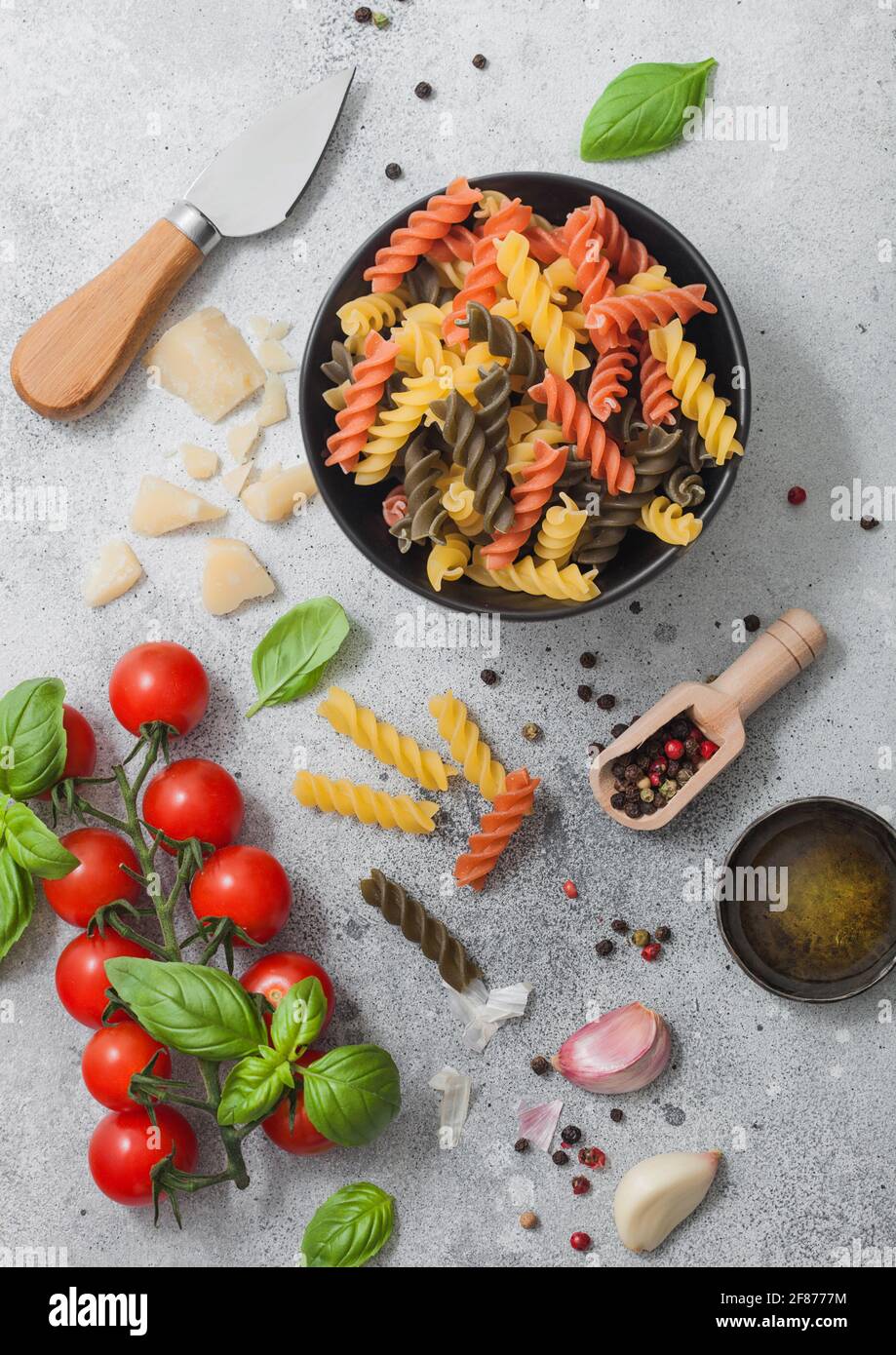 Fresh raw tricolore fusilli pasta in black bowl with cherry tomatoes ...