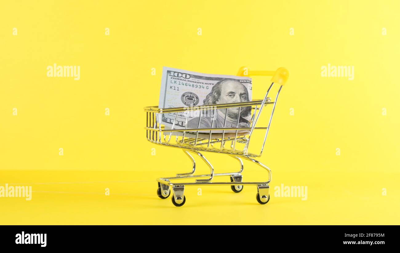 Shopping cart and one hundred dollar bill on a yellow background ...